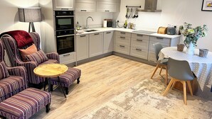 Cozinha moderna com eletrodomésticos embutidos, área de refeições com mesa redonda e um espaço de estar com sofás listrados e um cobertor vermelho.