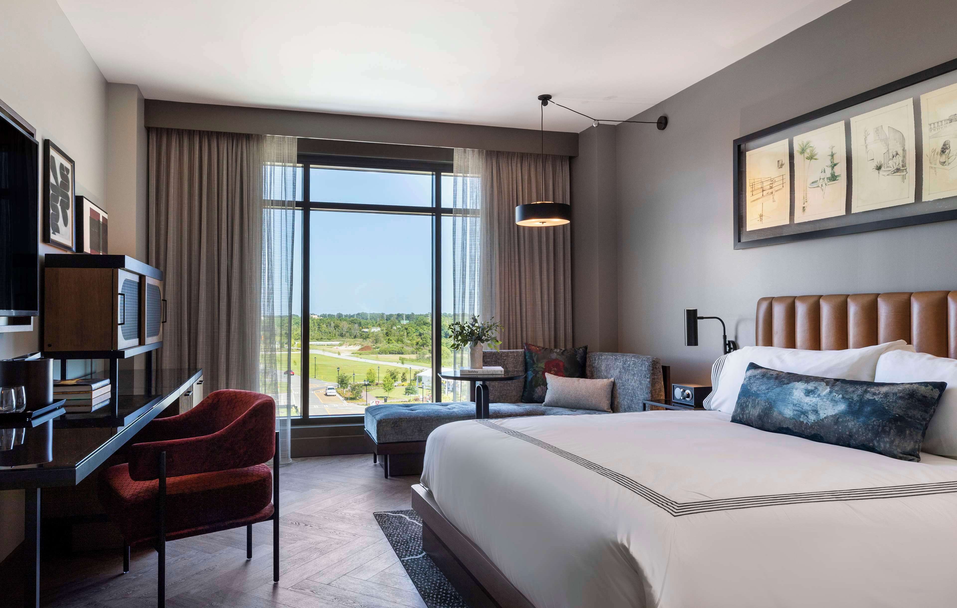 Quarto de hotel com cama grande, escrivaninha com cadeira, sofá e vista para o exterior.
