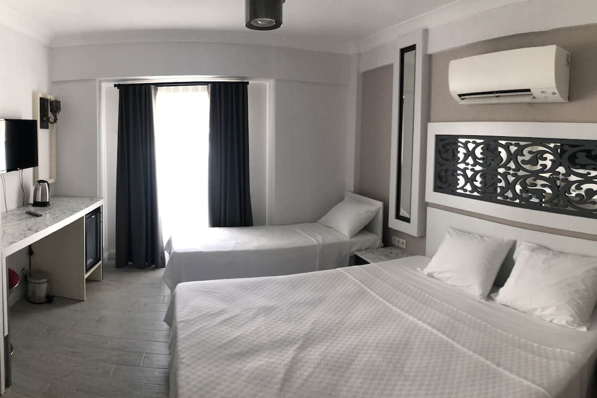 Quarto de hotel com cama, escrivaninha, cadeira, janela com cortinas, ar condicionado e painel decorativo.