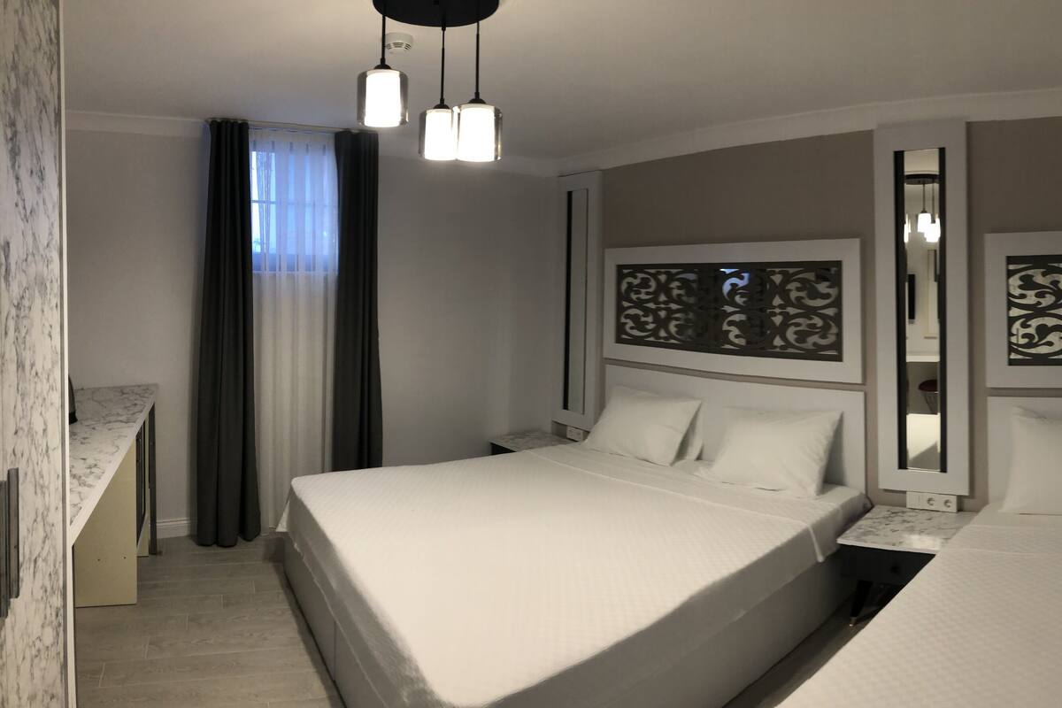 Quarto de hotel moderno com uma cama grande, mesas de cabeceira, uma escrivaninha e um espelho.