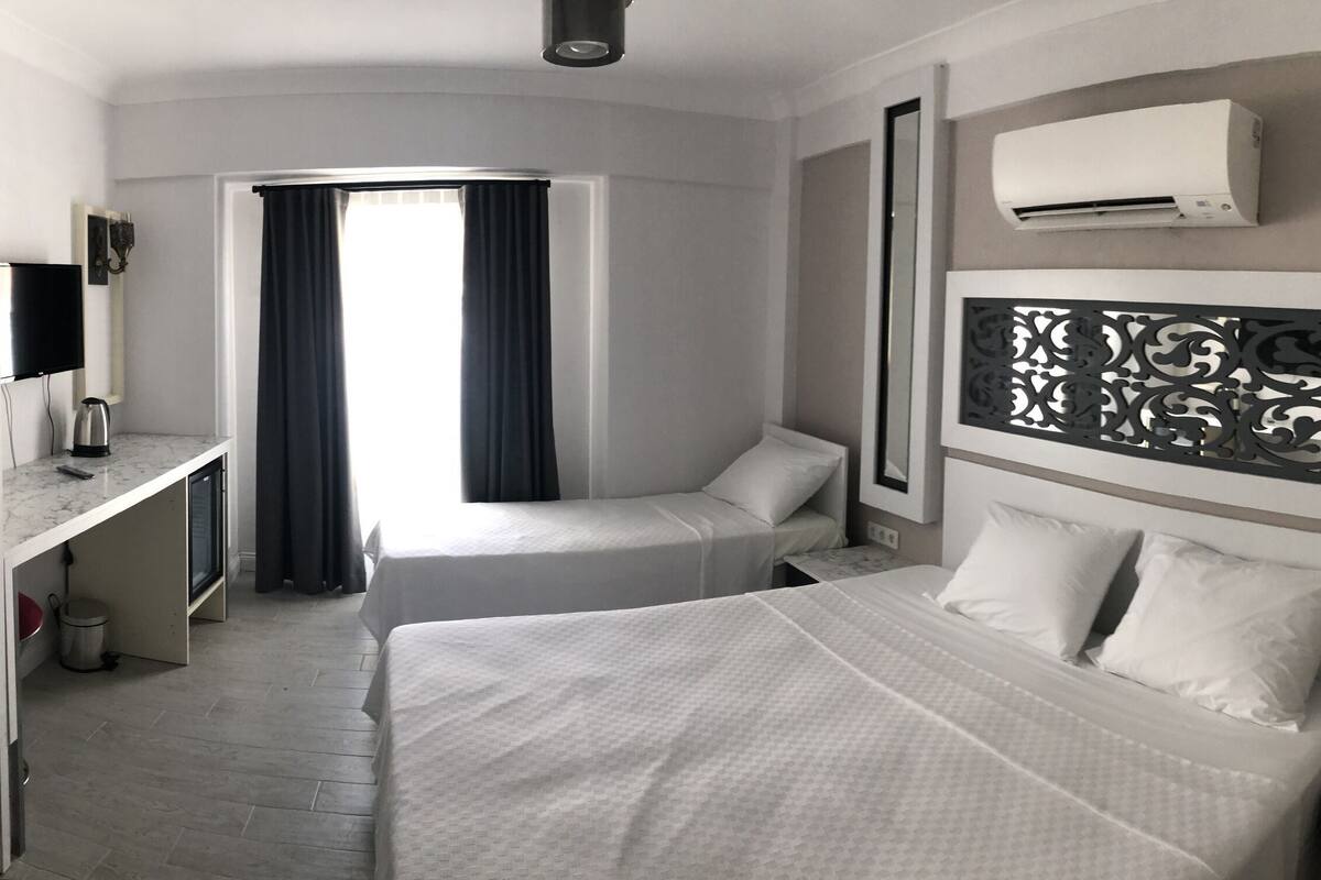 Quarto de hotel com uma cama, uma escrivaninha, uma cadeira, uma televisão e um aparelho de ar condicionado.