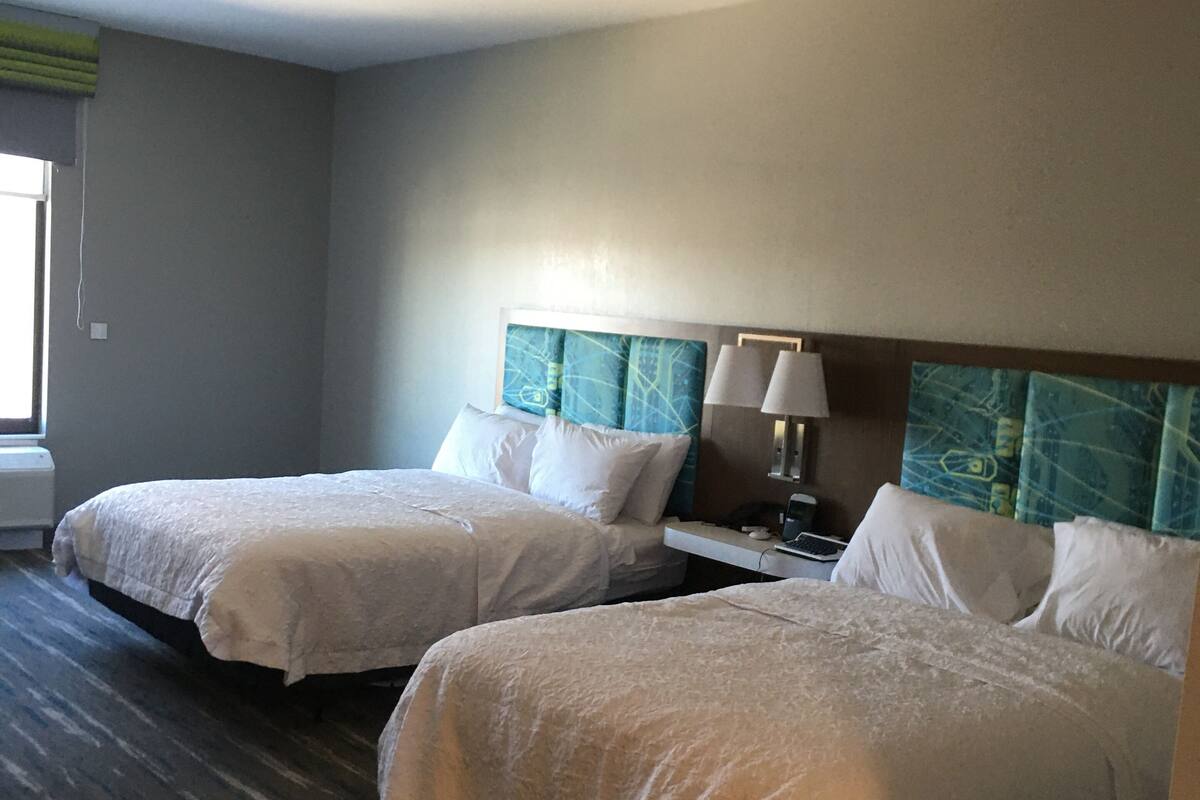 Quarto de hotel com duas camas, uma mesa de cabeceira e uma janela.