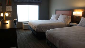 Quarto de hotel com duas camas, uma escrivaninha e uma janela.