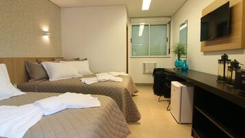 Quarto de hotel com duas camas, uma escrivaninha, televisão e um pequeno frigorífico.