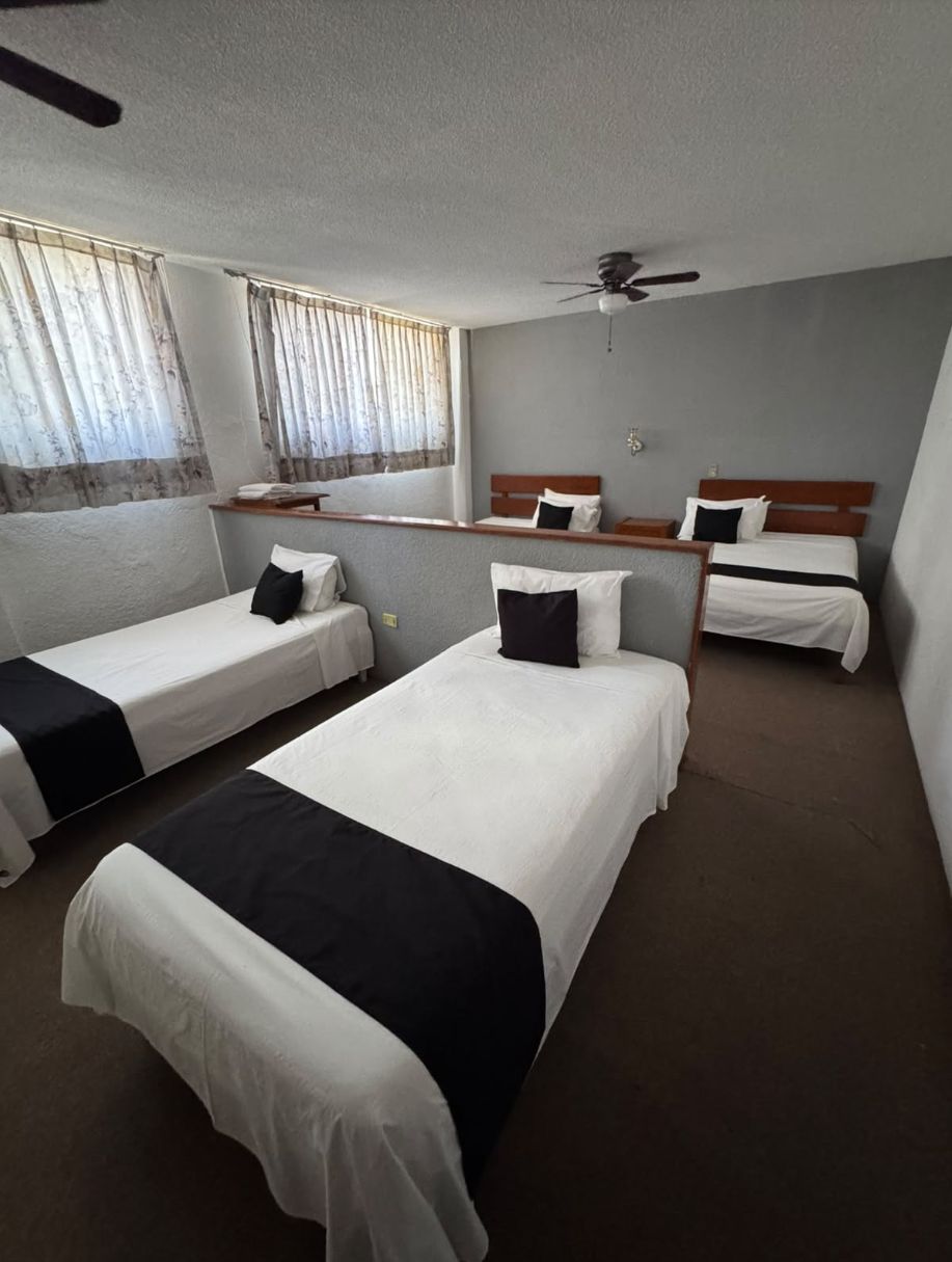 Quarto de hotel com duas camas de solteiro, ventilador de teto e janela com cortinas.