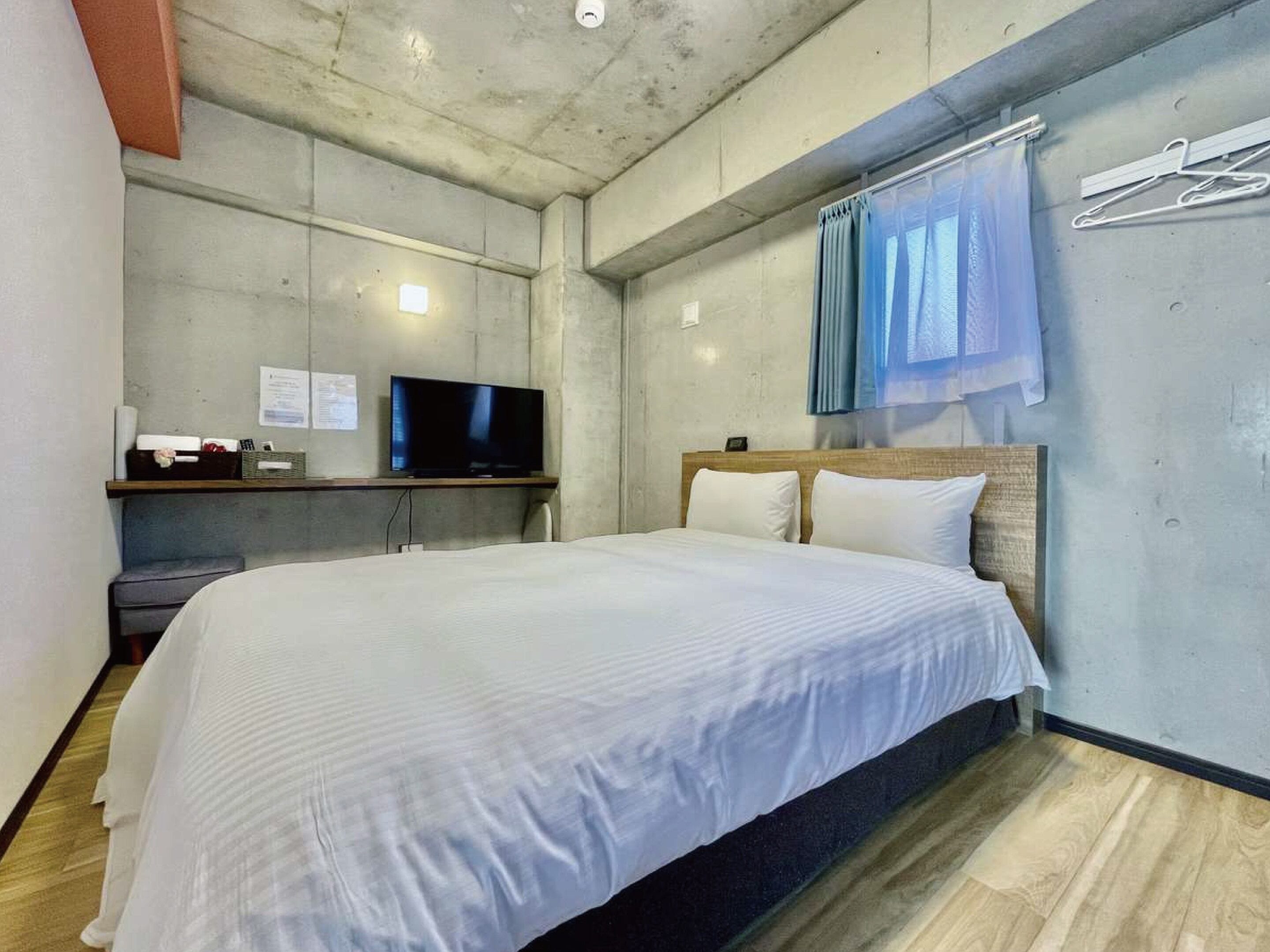 Quarto de hotel com uma cama grande, televisão de tela plana, escrivaninha com computador e janela com cortinas.