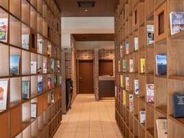 Um hall de hotel com estantes de madeira cheias de livros, um balcão de recepção e um chão ladrilhado.