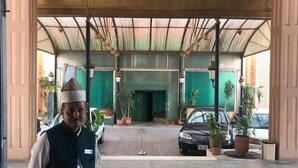 Uma entrada coberta com um carro estacionado, plantas em vasos e uma pessoa na porta.