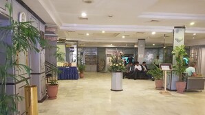 Um lobby com balcão de recepção, plantas em vasos e área com padrão azul.