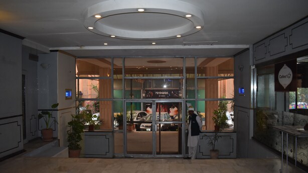 Entrada de hotel com porta de vidro, plantas em vasos e placa para o Cafe 10.