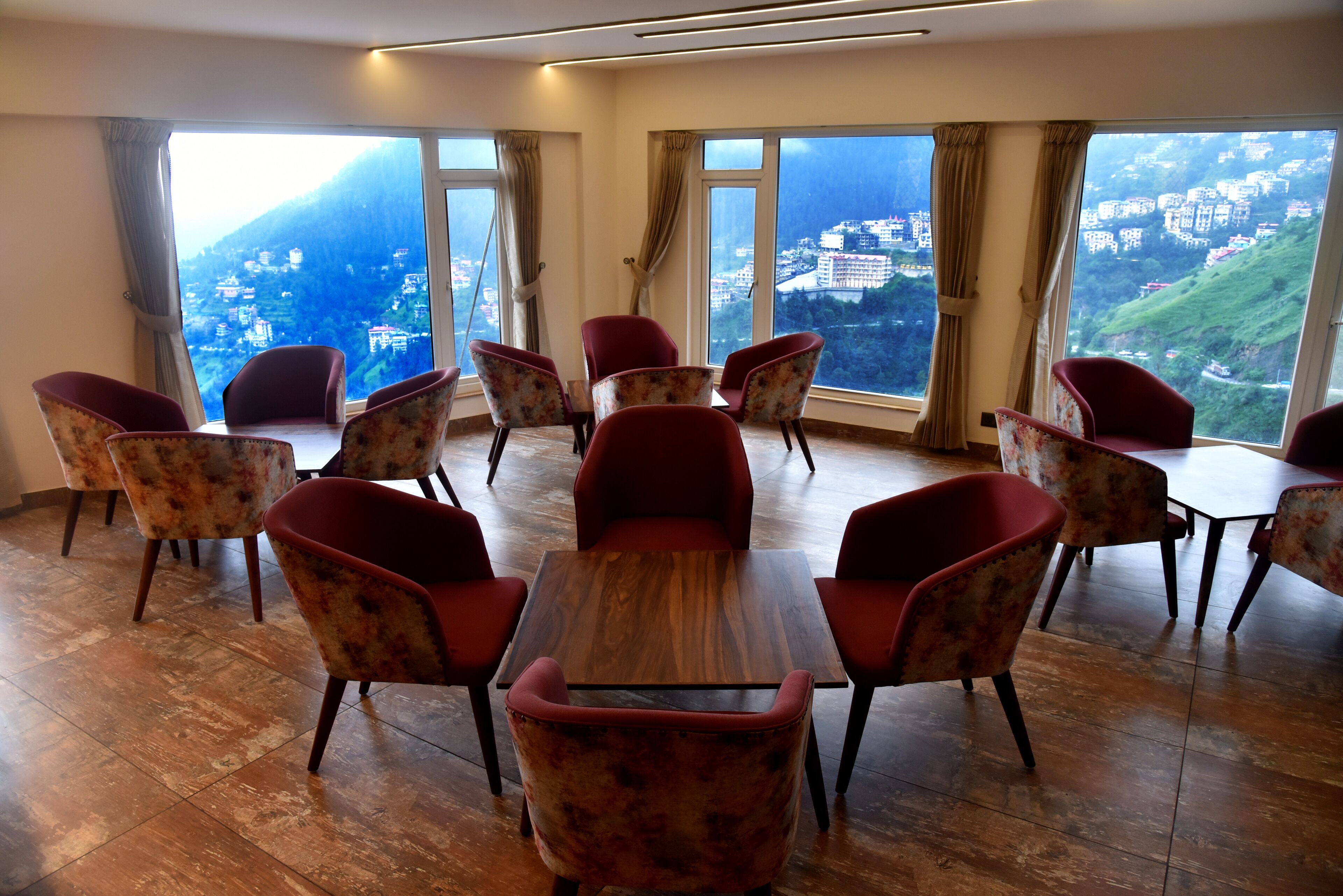 Uma sala de conferências com mesa de madeira e cadeiras vermelhas, janelas amplas com vista para uma paisagem montanhosa.