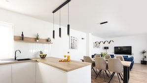 Cozinha moderna com bancada de madeira, armários brancos e área de jantar com sofá azul e televisão.