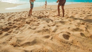 Uma praia com três pessoas em pé na areia, céu claro e o oceano ao fundo.