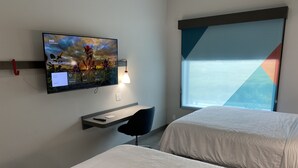 Quarto de hotel com duas camas, uma televisão presa à parede, uma mesa com cadeira e uma janela com vista.