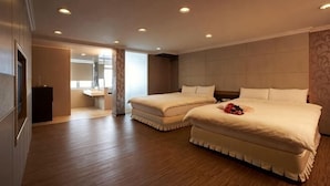 Quarto de hotel com duas camas, piso de madeira, banheiro com espelho e uma pequena escrivaninha.