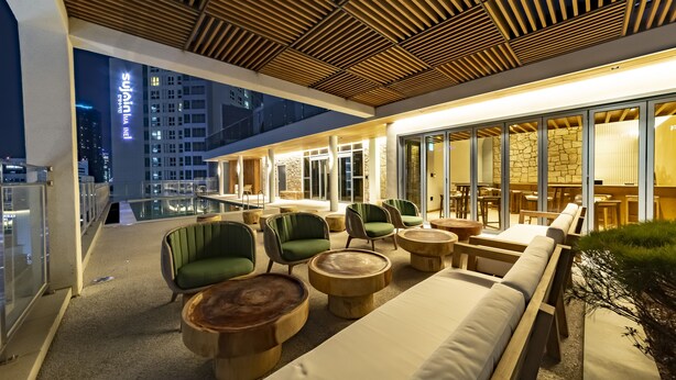 Uma área de estar ao ar livre com assentos, piscina e vista para o horizonte da cidade à noite.