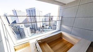 Uma casa de banho moderna com uma banheira de madeira, uma janela com vista para a paisagem urbana e para edifícios altos.