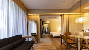 Quarto de hotel moderno com sofá, mesa de madeira redonda e área de refeições com cadeiras.