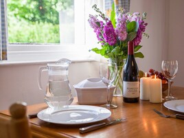 Mesa posta com pratos, jarra, garrafa de vinho, velas e um vaso com flores.