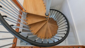 Escadaria em espiral com degraus de madeira e corrimãos de metal.