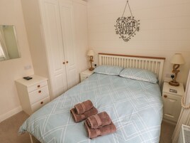 Quarto com cama, duas mesas de cabeceira, cômoda, espelho e um objeto decorativo na parede.
