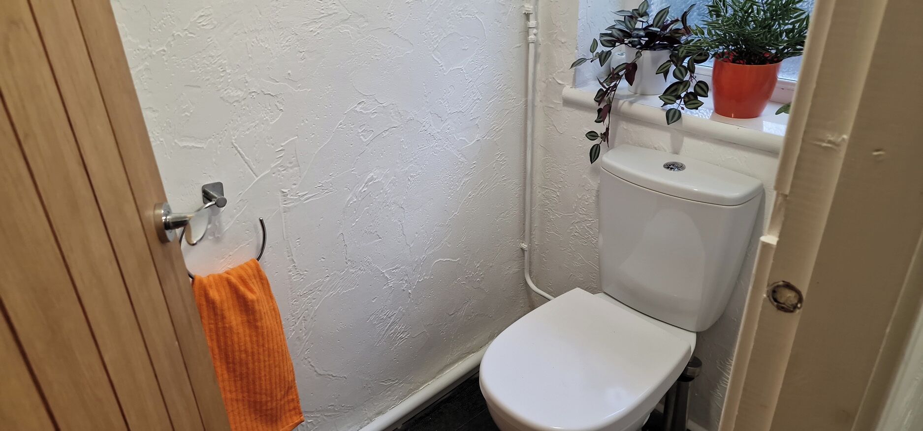 Um banheiro pequeno com vaso sanitário branco, porta de madeira e toalha pendurada na porta.
