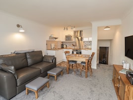 Uma sala de estar moderna com um sofá de couro marrom, uma mesa de jantar de madeira com duas cadeiras e um pequeno armário de madeira.