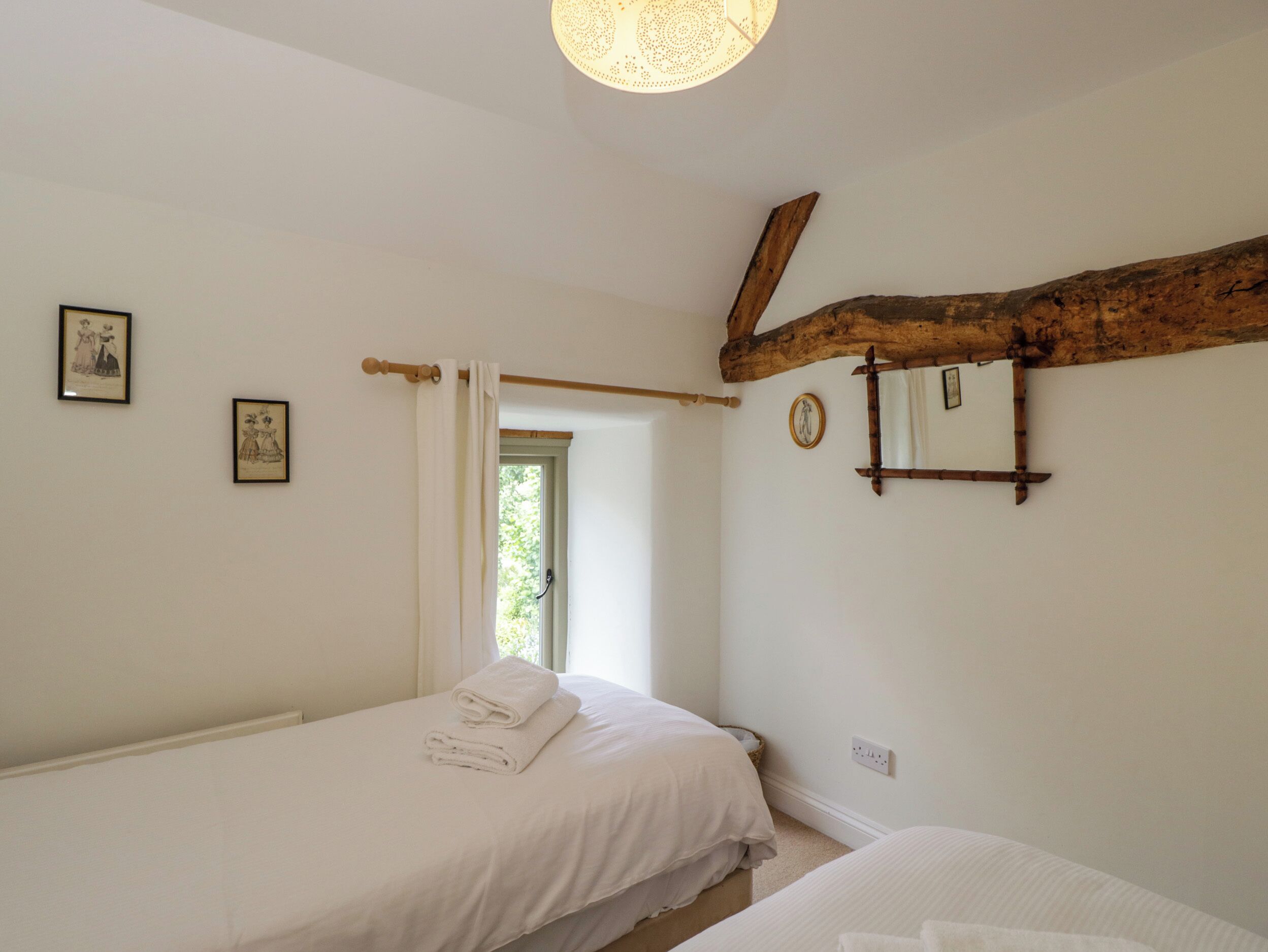 Quarto com duas camas, teto com vigas de madeira e janela com vista para o verde.