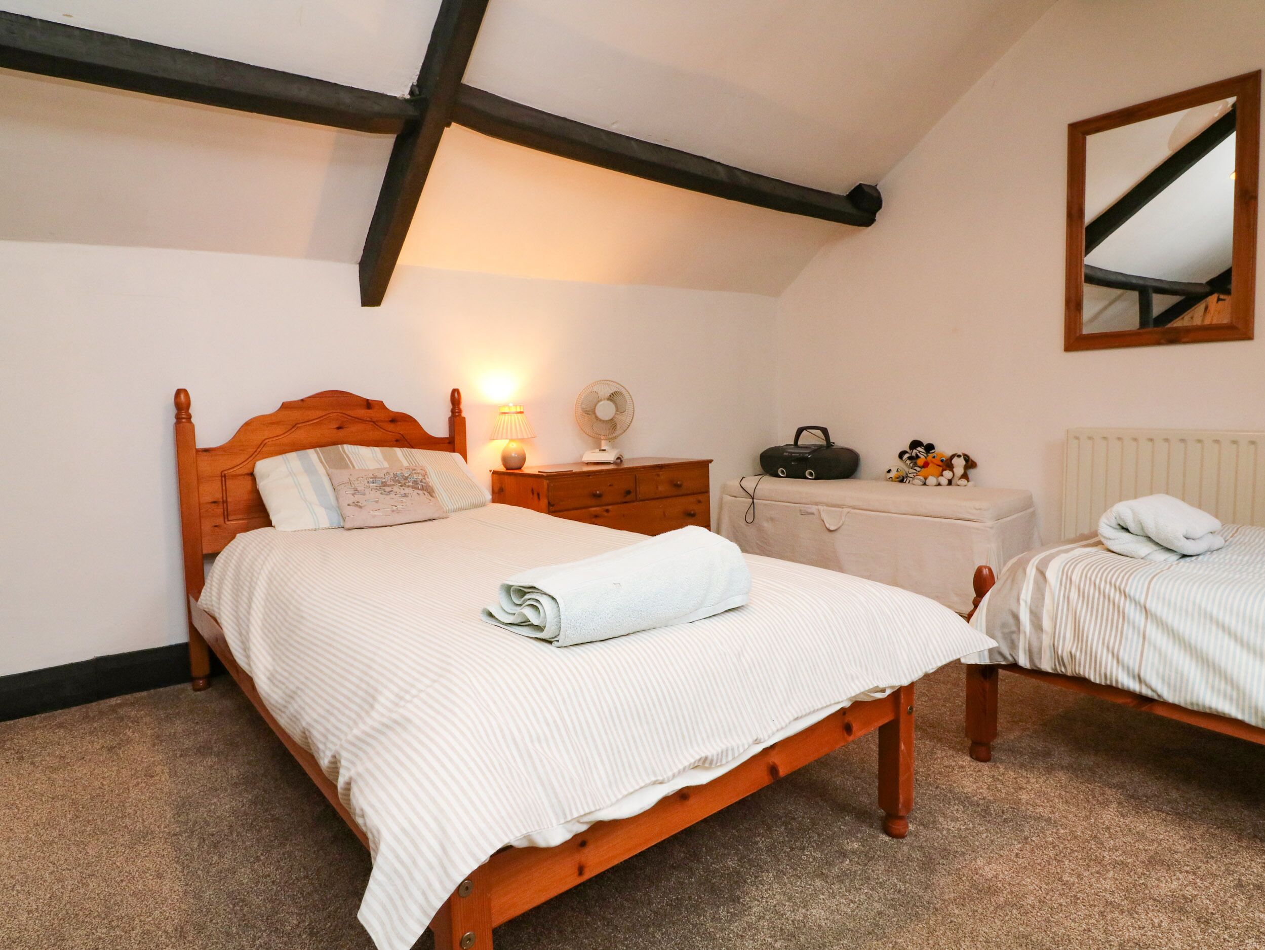 Quarto com cama de madeira, mesa de cabeceira com abajur, cômoda e espelho na parede.