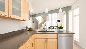 Cozinha moderna com armários de madeira, lava-louças de aço inoxidável e iluminação pendente.