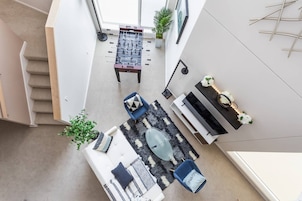 Uma sala de estar moderna com mesa de pebolim, sofá, mesa de centro e uma pequena mesa lateral com objetos decorativos.