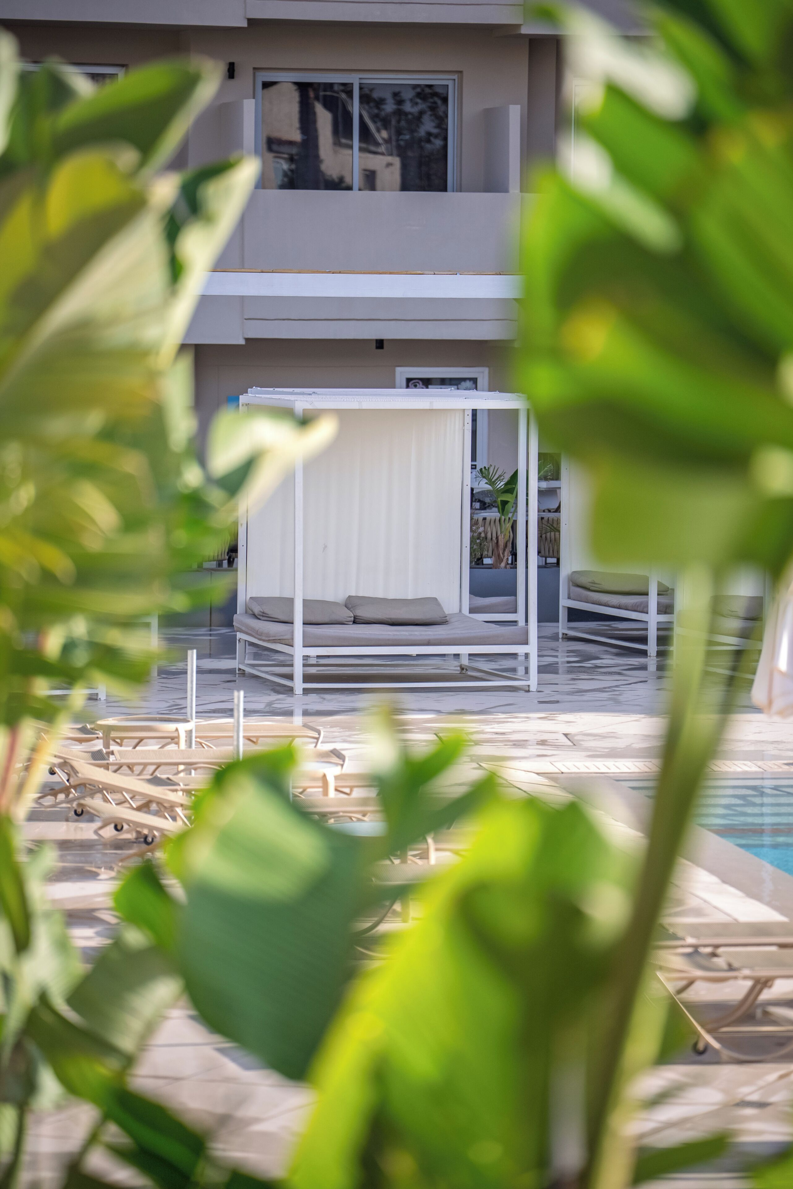 Uma área de estar moderna ao ar livre, com estrutura branca, cadeiras de apoio e piscina.