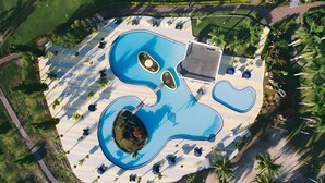 Vista aérea de uma área de piscina com várias piscinas, espreguiçadeiras e palmeiras.