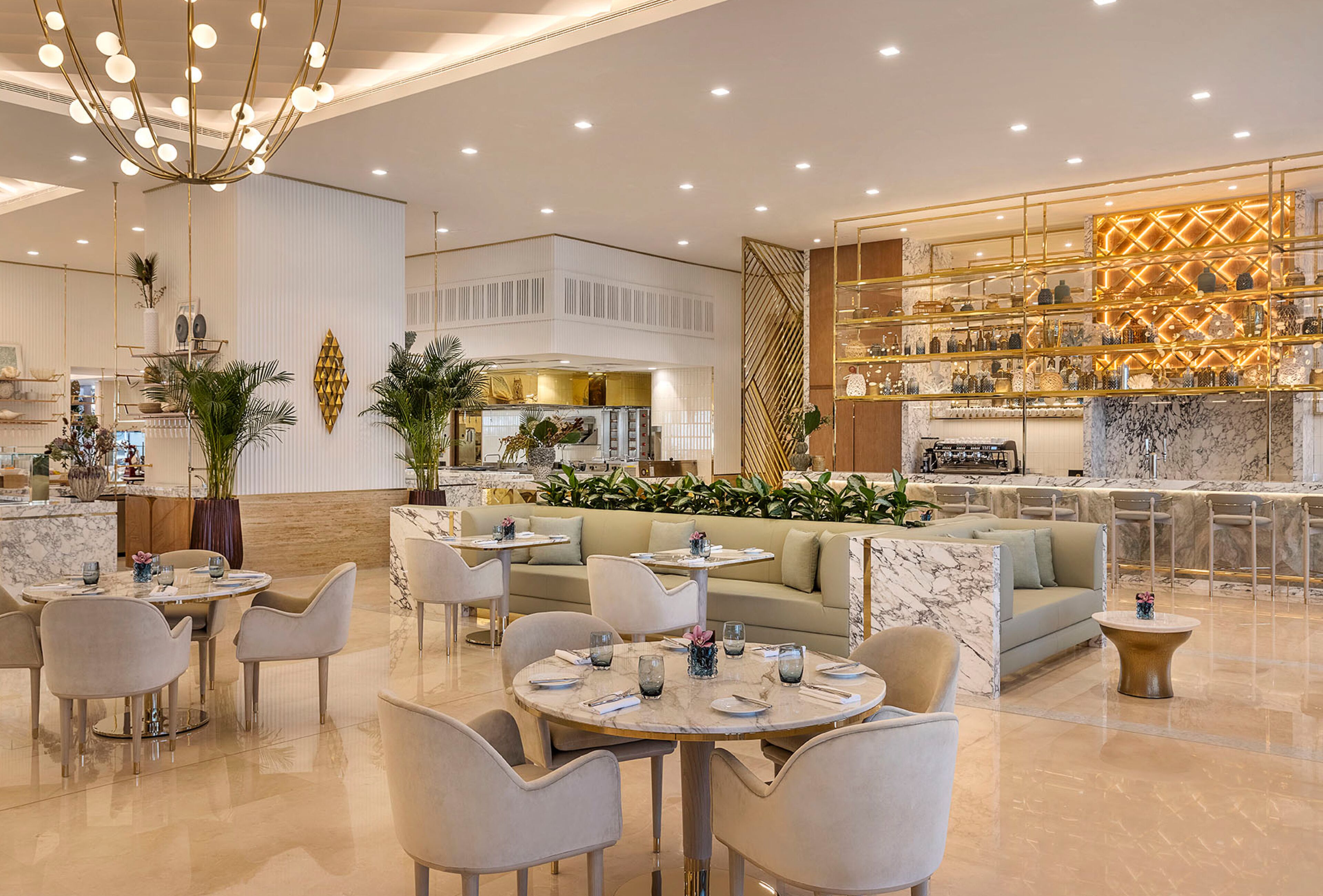 Um hall de hotel moderno com mesas redondas, sofás e um bar com bancadas de mármore.