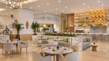 Um hall de hotel moderno com mesas redondas, sofás e um bar com bancadas de mármore.