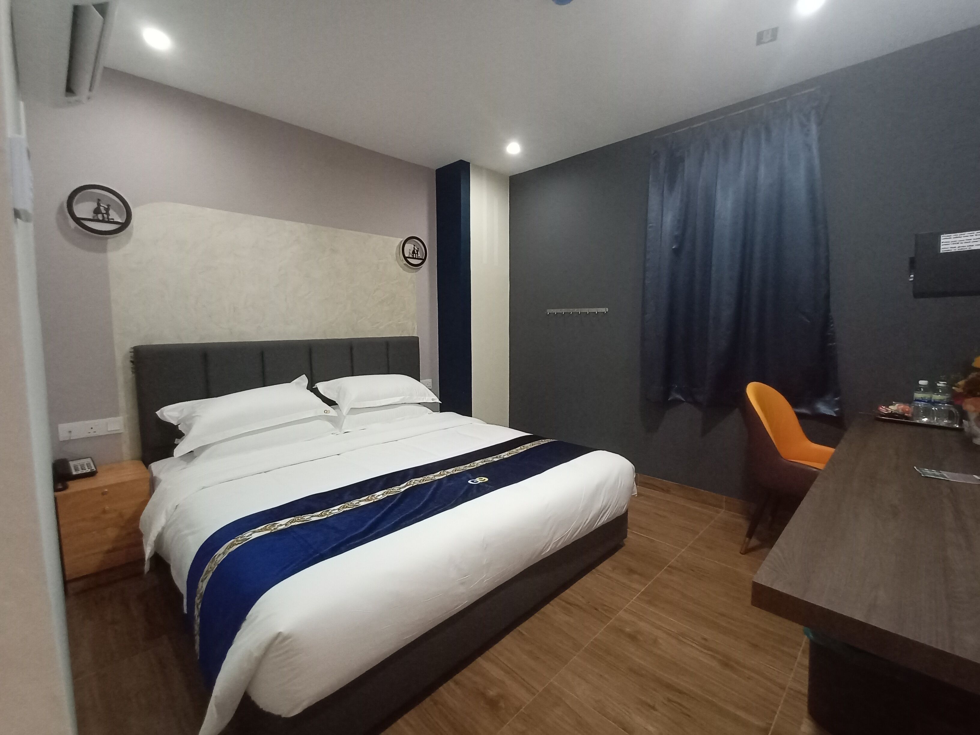 Quarto de hotel com cama, escrivaninha, cadeira e janela com cortinas.