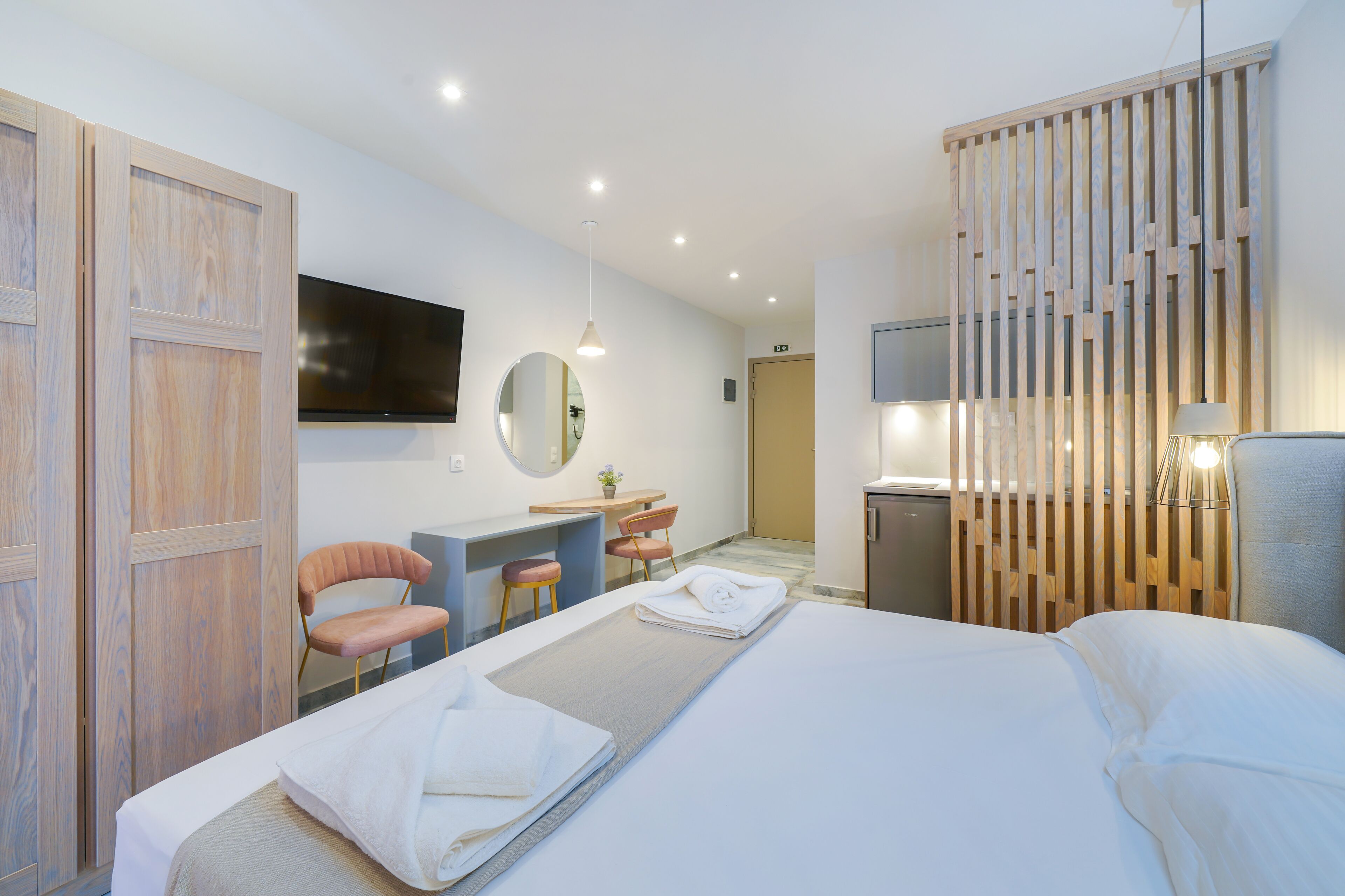 Quarto de hotel com cama, escrivaninha, cadeira, espelho e televisão.