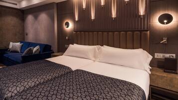 Quarto de hotel com uma cama grande, um sofá azul e uma luminária fixada na parede.