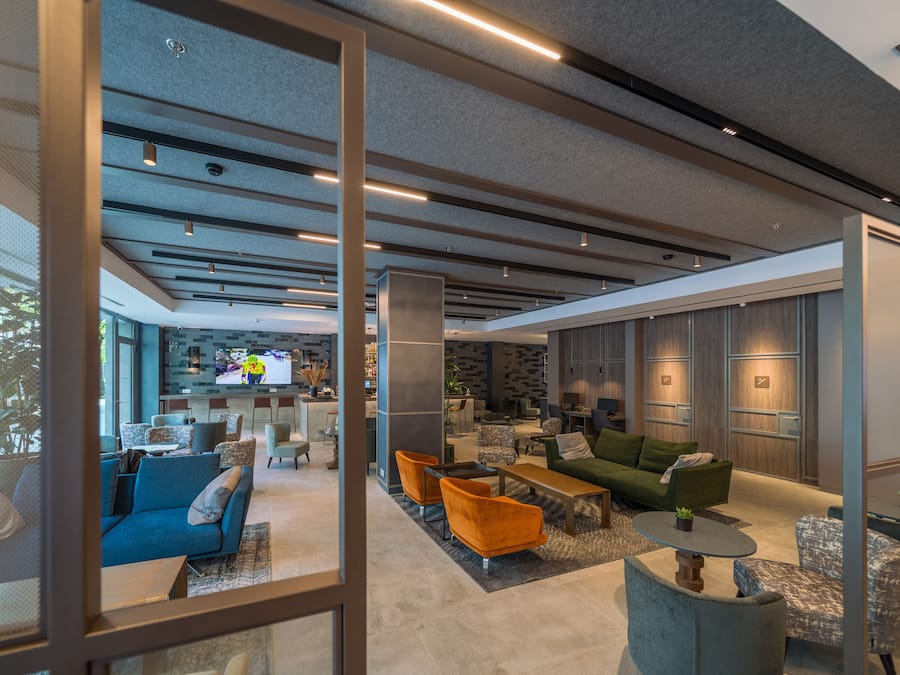 Um hall moderno de hotel com área de estar, bar e uma tela de televisão.