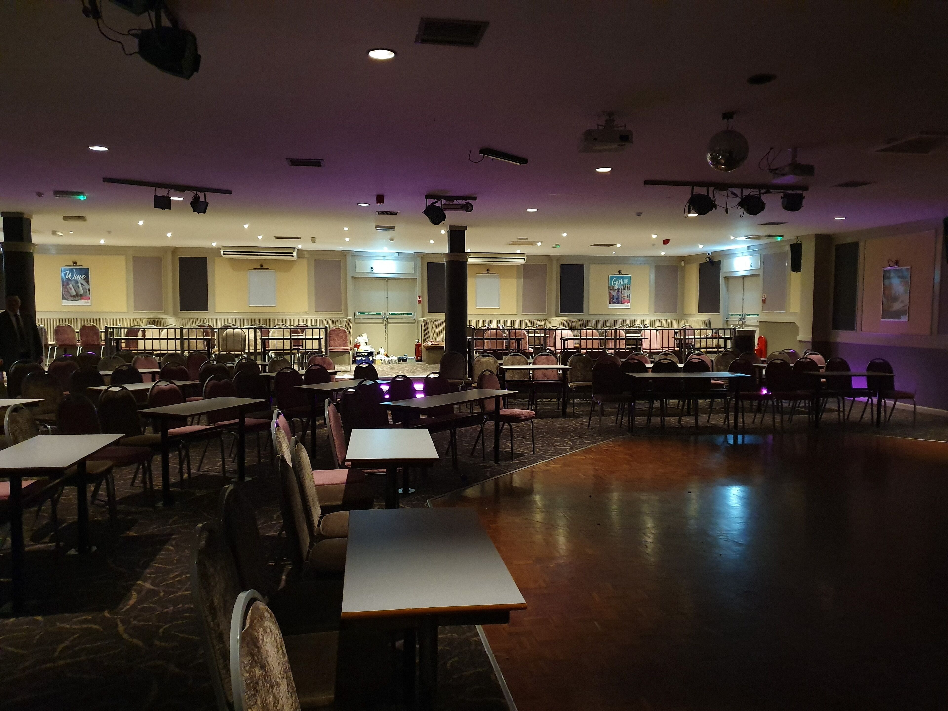 Uma sala de conferências com mesas e cadeiras dispostas em fileiras, um palco com um púlpito e uma tela grande.