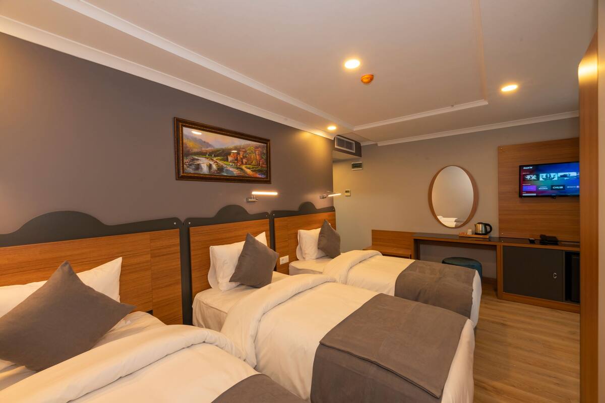 Quarto de hotel com duas camas, uma escrivaninha, uma televisão e um quadro na parede.