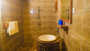 Uma casa de banho com lavatório em madeira de barril, um porta-toalhas com toalha branca, chuveiro com chuveiro manual e prateleira de madeira com copos azuis.