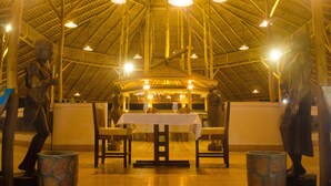 Um restaurante com teto de madeira alto, mesas preparadas para refeições e vasos de pedra.