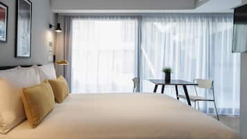 Quarto de hotel moderno com uma cama grande, uma mesinha, cadeiras e uma televisão.