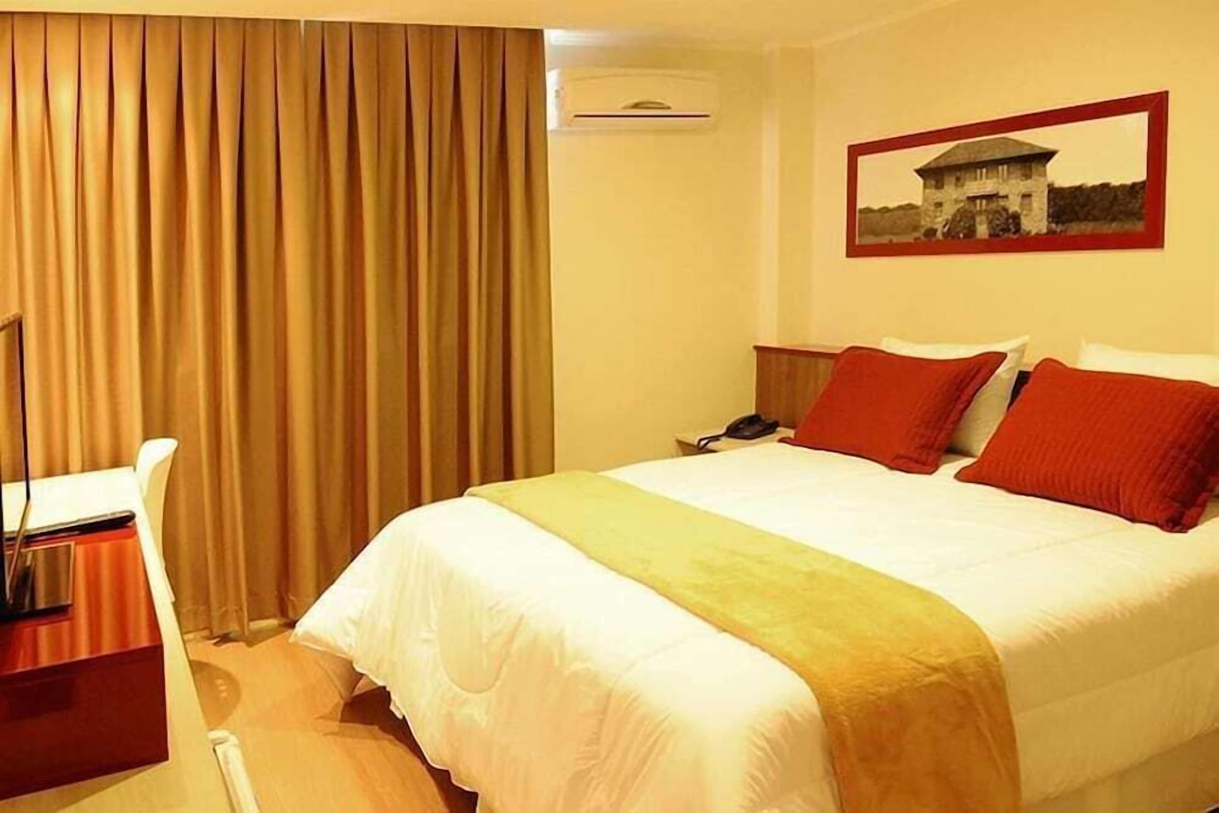 Quarto de hotel com uma cama, uma escrivaninha, uma cadeira, ar condicionado e um quadro na parede.