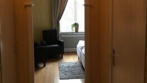 Corredor que dá para um quarto com janela, uma cadeira e uma cama.