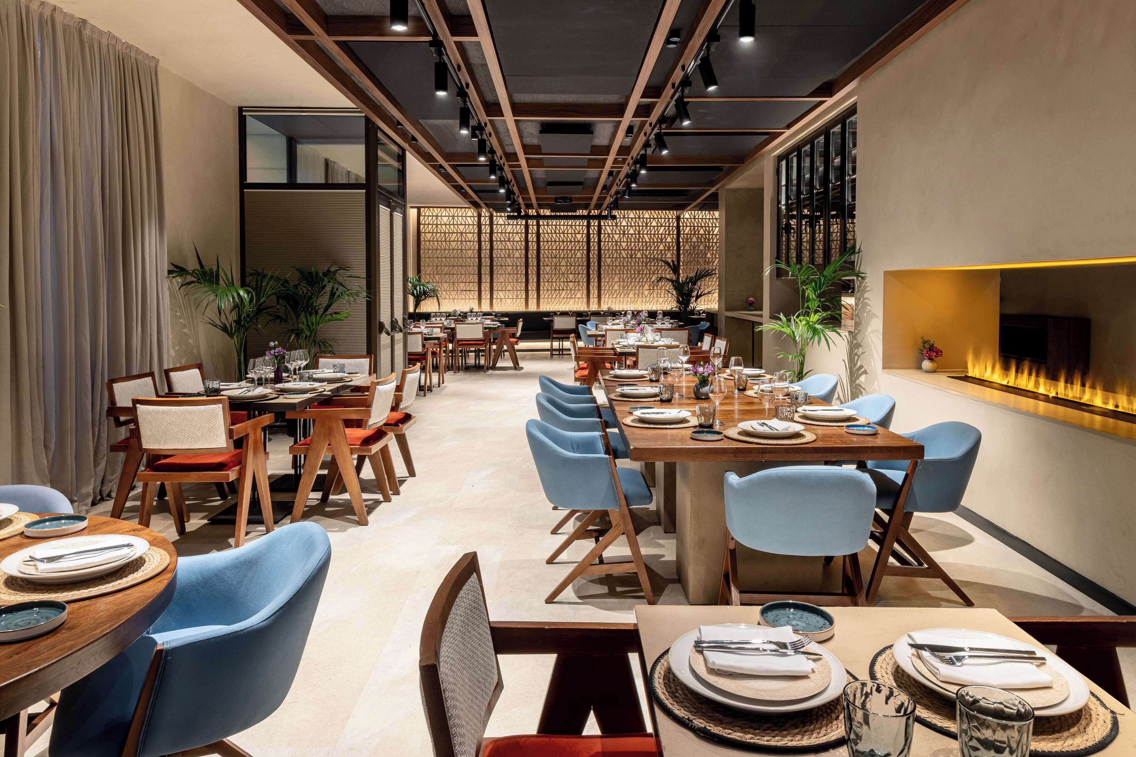 Uma sala de jantar moderna com várias mesas e cadeiras, uma parede decorativa e uma lareira.
