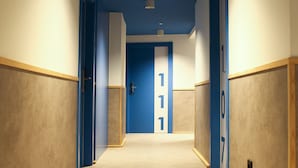 Corredor com portas azuis e paredes bege, que leva a uma porta com o número 111.
