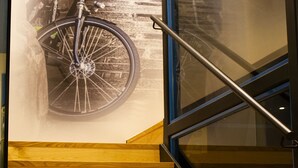 Uma escadaria com degraus de madeira e corrimãos de metal, que leva a um quarto com um grande cartaz de uma bicicleta.