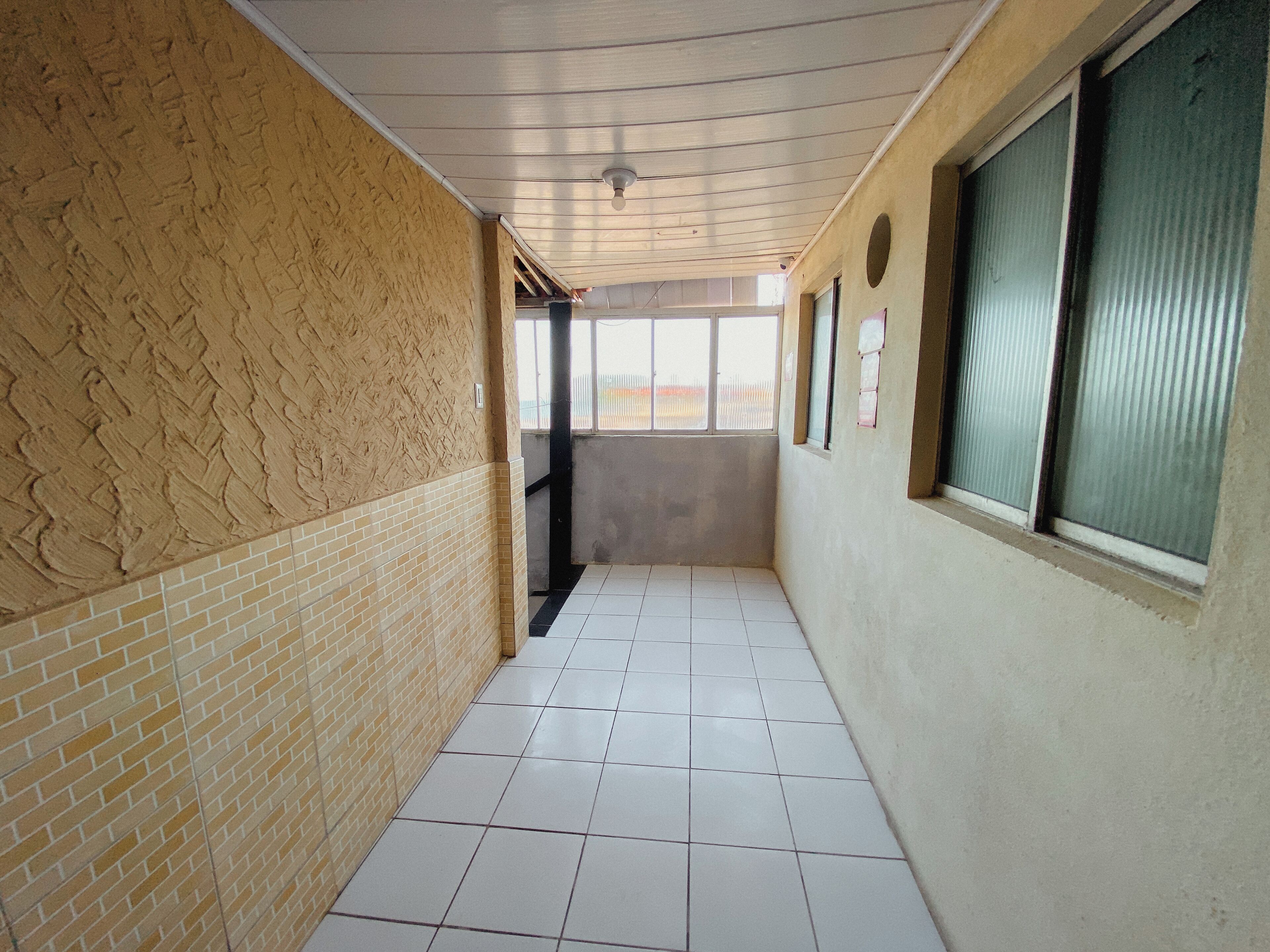 Um corredor com chão de azulejos, uma parede de tijolos de um lado e uma parede lisa do outro.